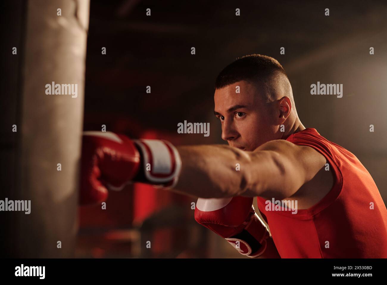 Young muscular man in red boxing gloves kicking punching box during training while practicing ...