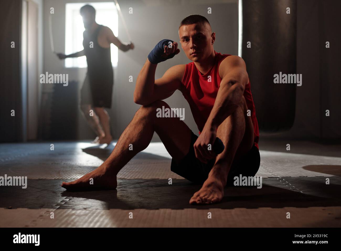 Young barefoot athlete in sportswear sitting on the floor of gym and ...