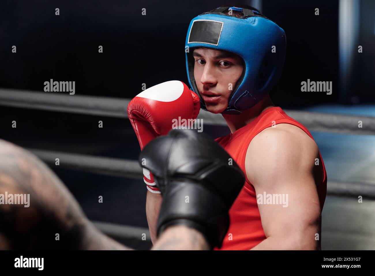 Young muscular man in red vest and boxing gloves and blue face shield ...