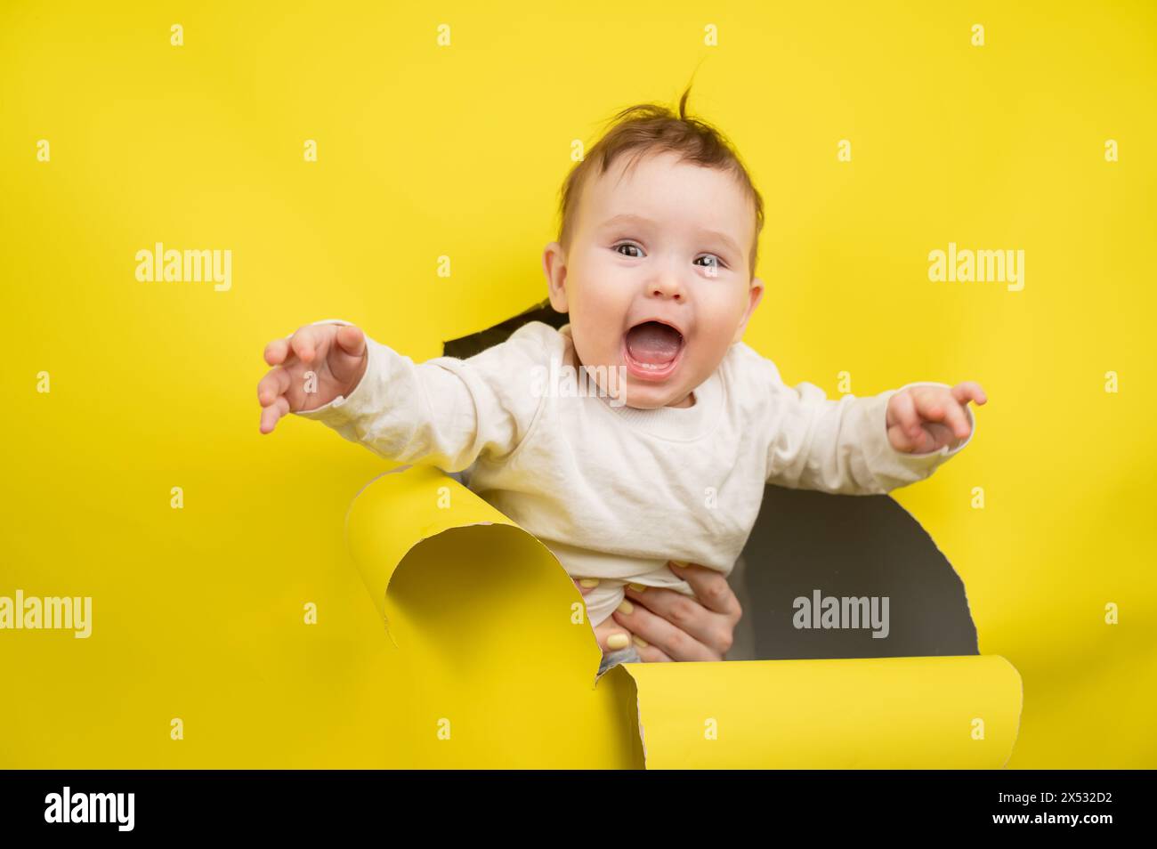 Cheerful baby rips and sticks out through yellow cardboard background ...