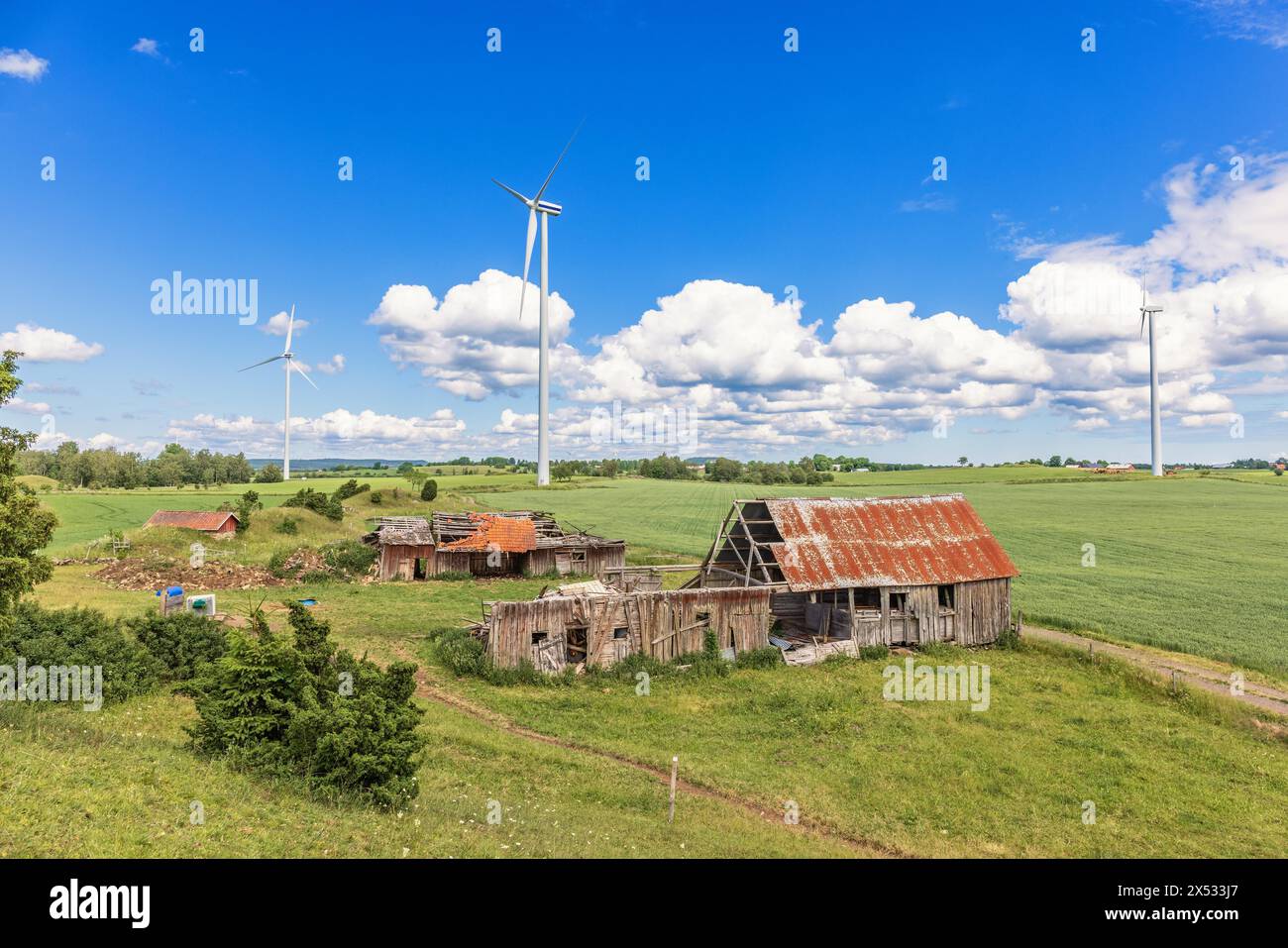 Old ruined farm in a rural landscape view with wind turbines on the fields in the summer, Sweden ...