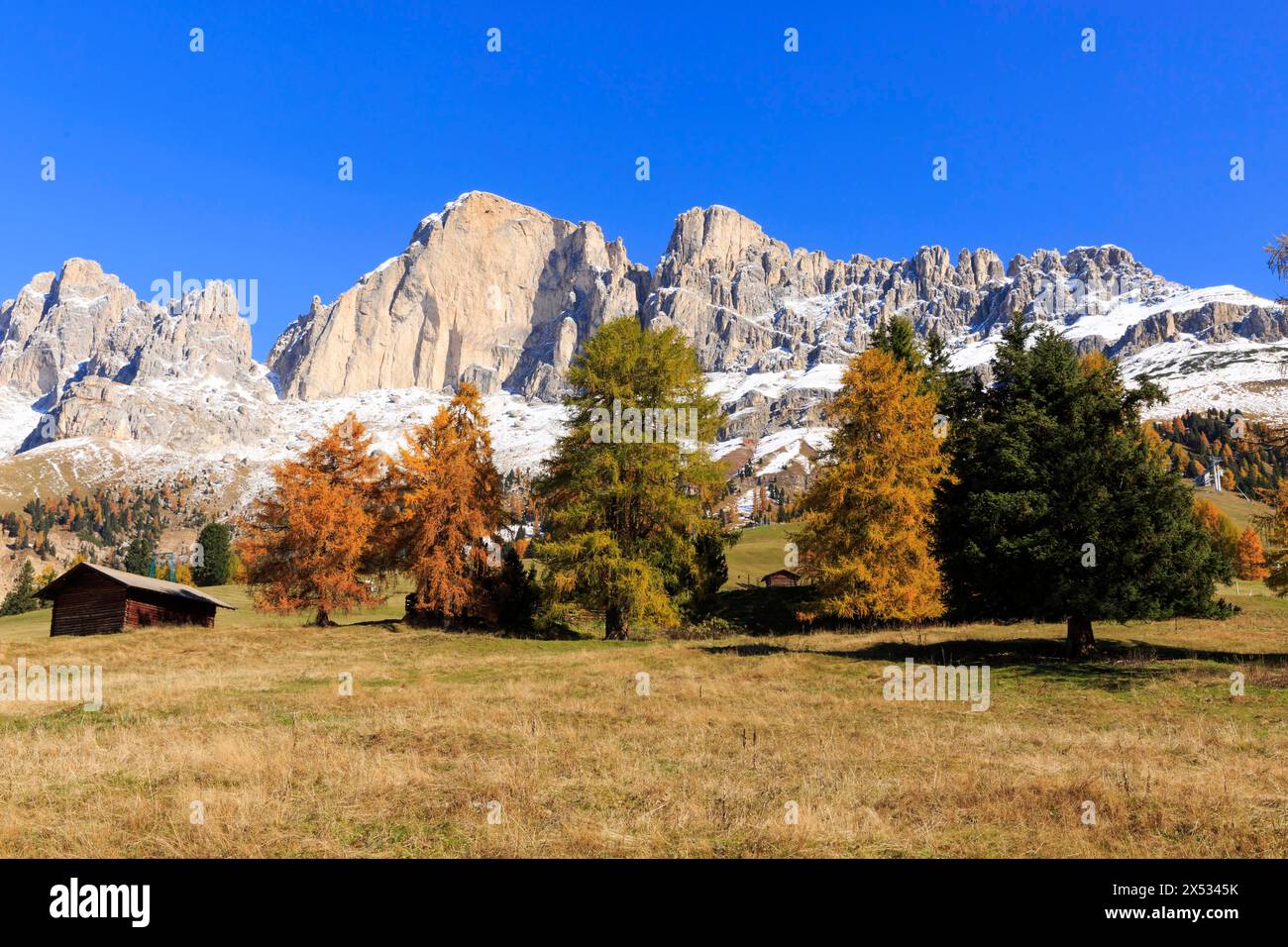 Snow on rocky peaks behind a meadow with a wooden hut in autumn, Italy ...