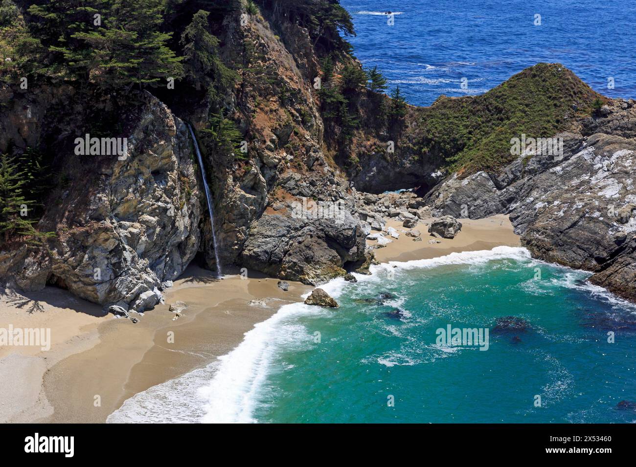 A powerful waterfall flows between rocky cliffs into the sea, Big Sur ...