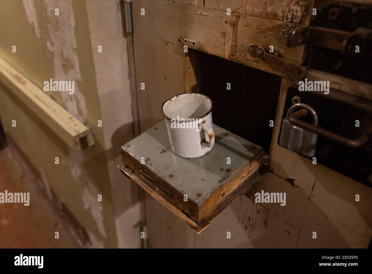 Rusted metal cup stands on the food hatch of a prison cell, former ...