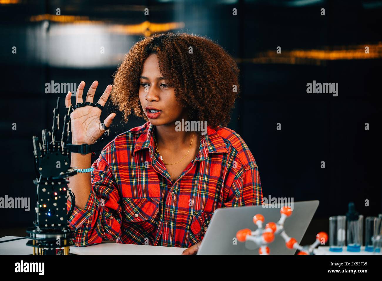 Portrait of a Black teenage student in a classroom learning about a robotic arm for her ...