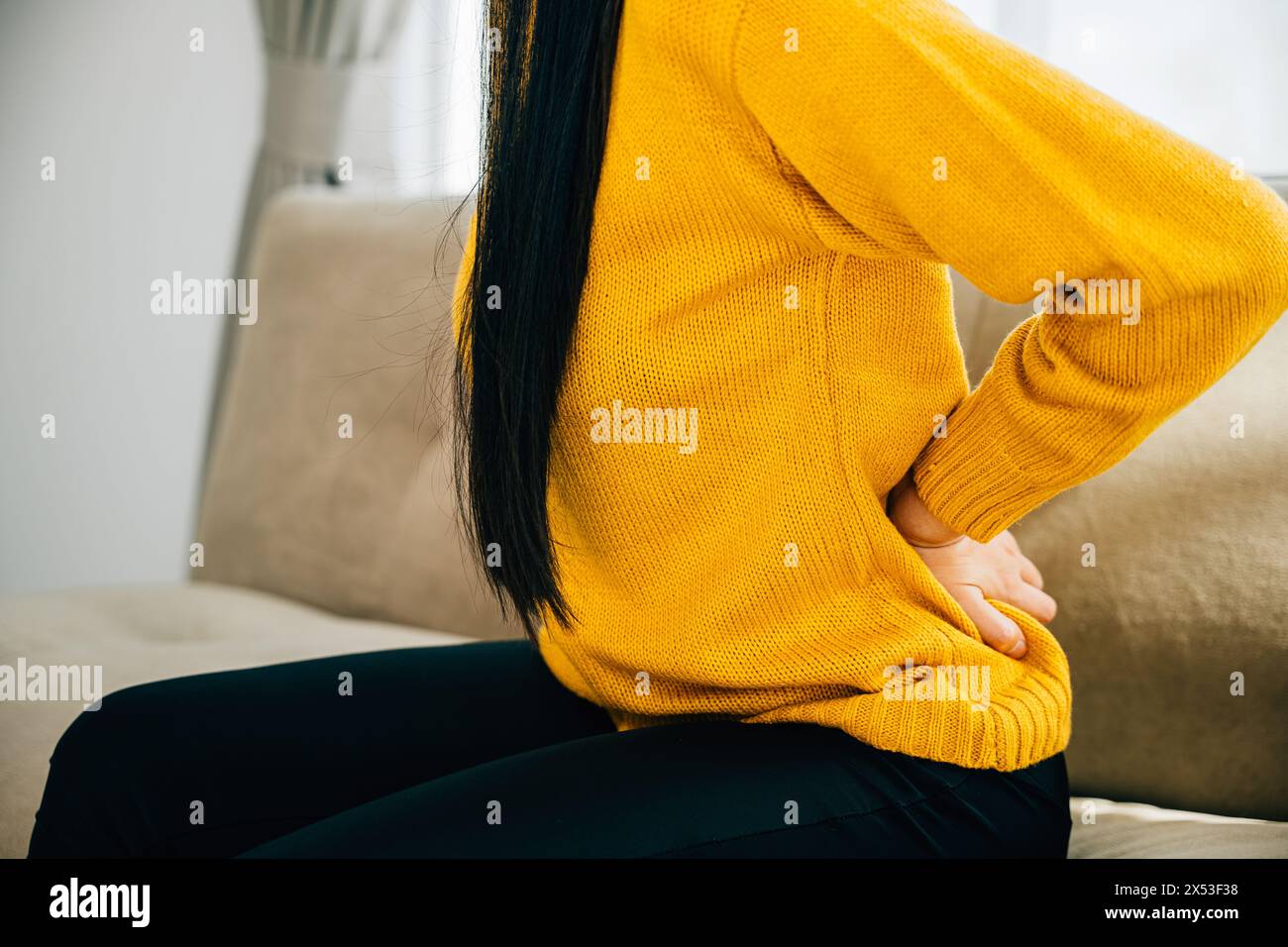 Asian woman holds her lower back in unbearable pain on a sofa Stock ...