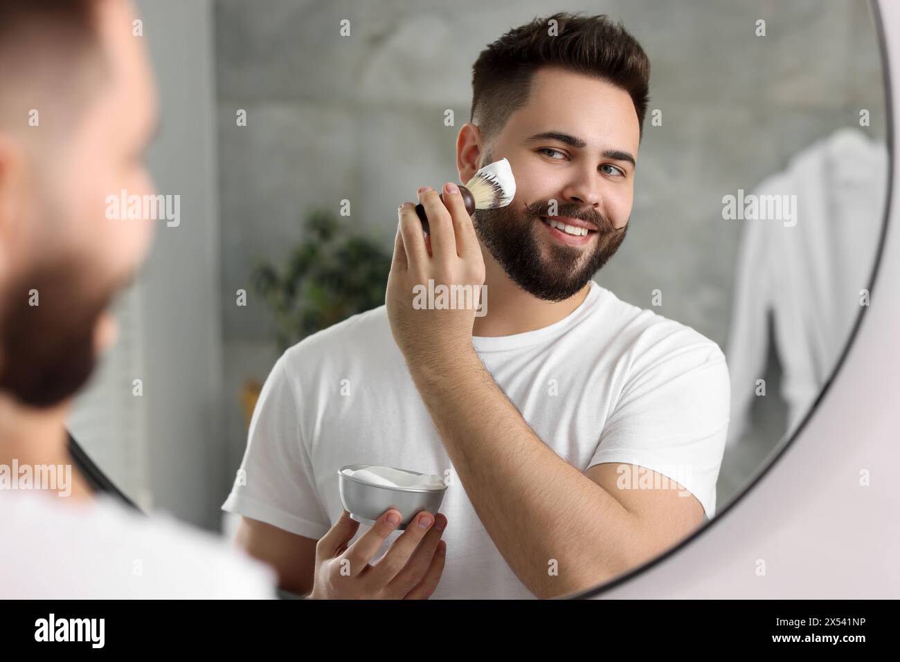 Handsome young man shaving beard near mirror in bathroom Stock Photo ...