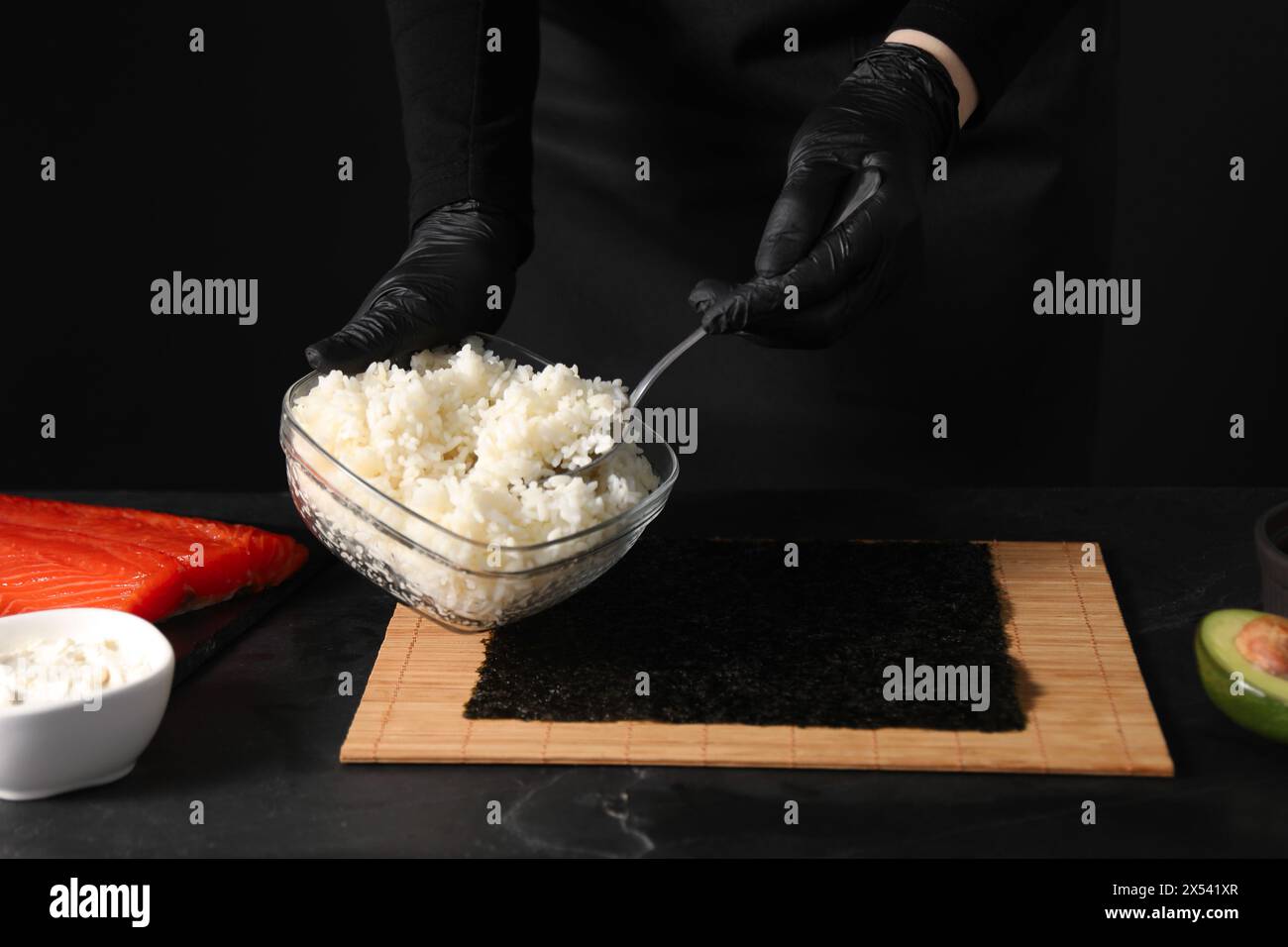 Chef in gloves taking cooked rice for sushi with spoon at dark table ...