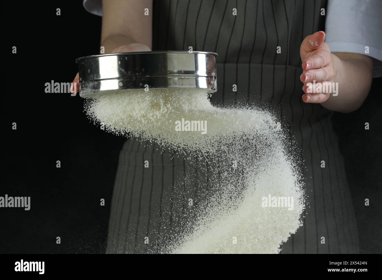 Woman sieving flour at table against black background, closeup Stock ...