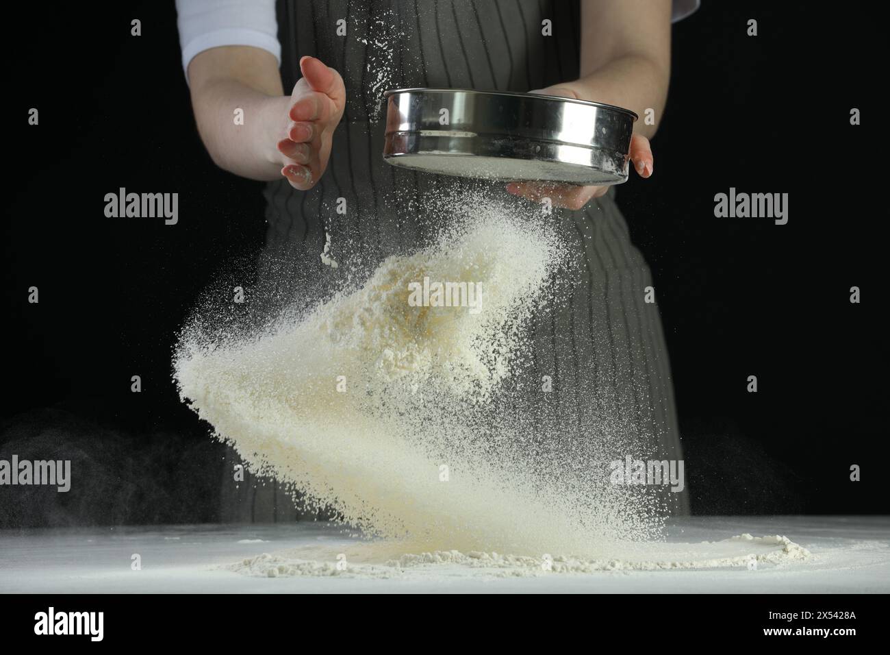 Woman sieving flour at table against black background, closeup Stock ...