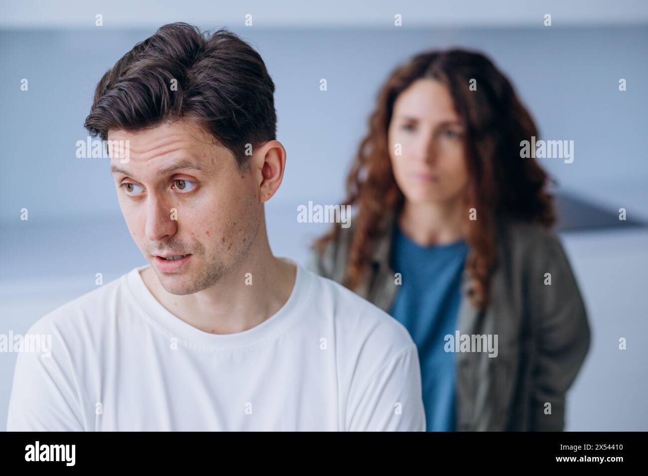 Man with concerned expression looks away while woman stands behind him ...
