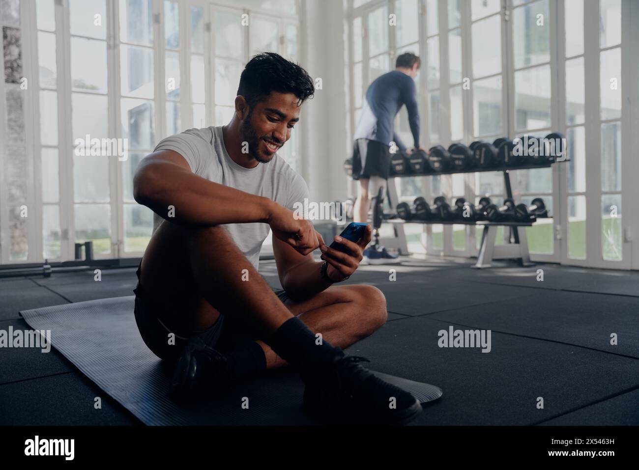 Two multiracial young men in sportswear smiling and using mobile phone ...