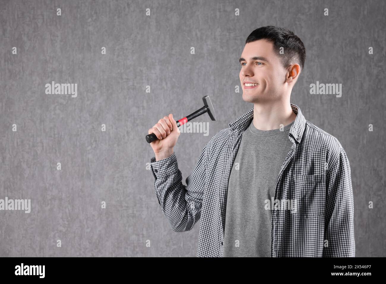 Young man holding hammer on grey background. Space for text Stock Photo ...