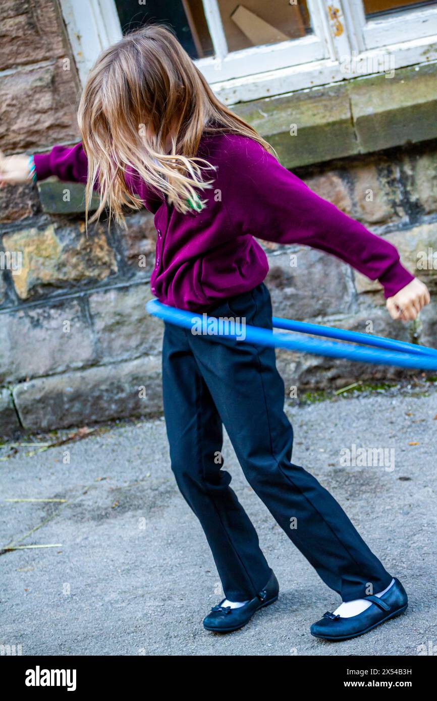 Primary school child playing with hoop outside in a school playground ...