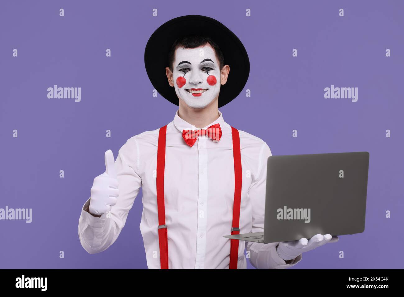 Funny mime artist with laptop showing thumbs up on purple background ...