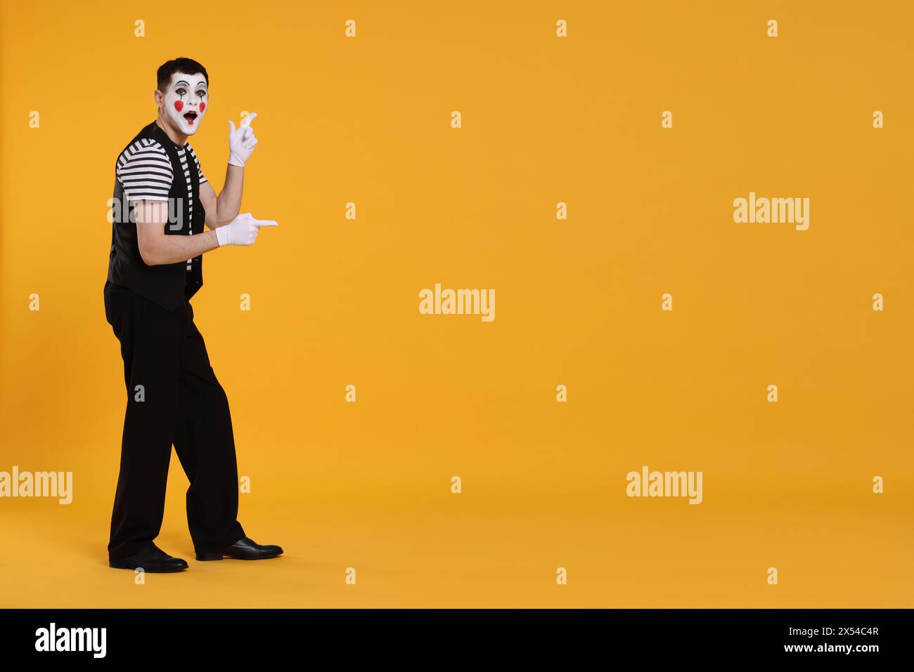 Funny mime artist pointing at something on orange background. Space for ...