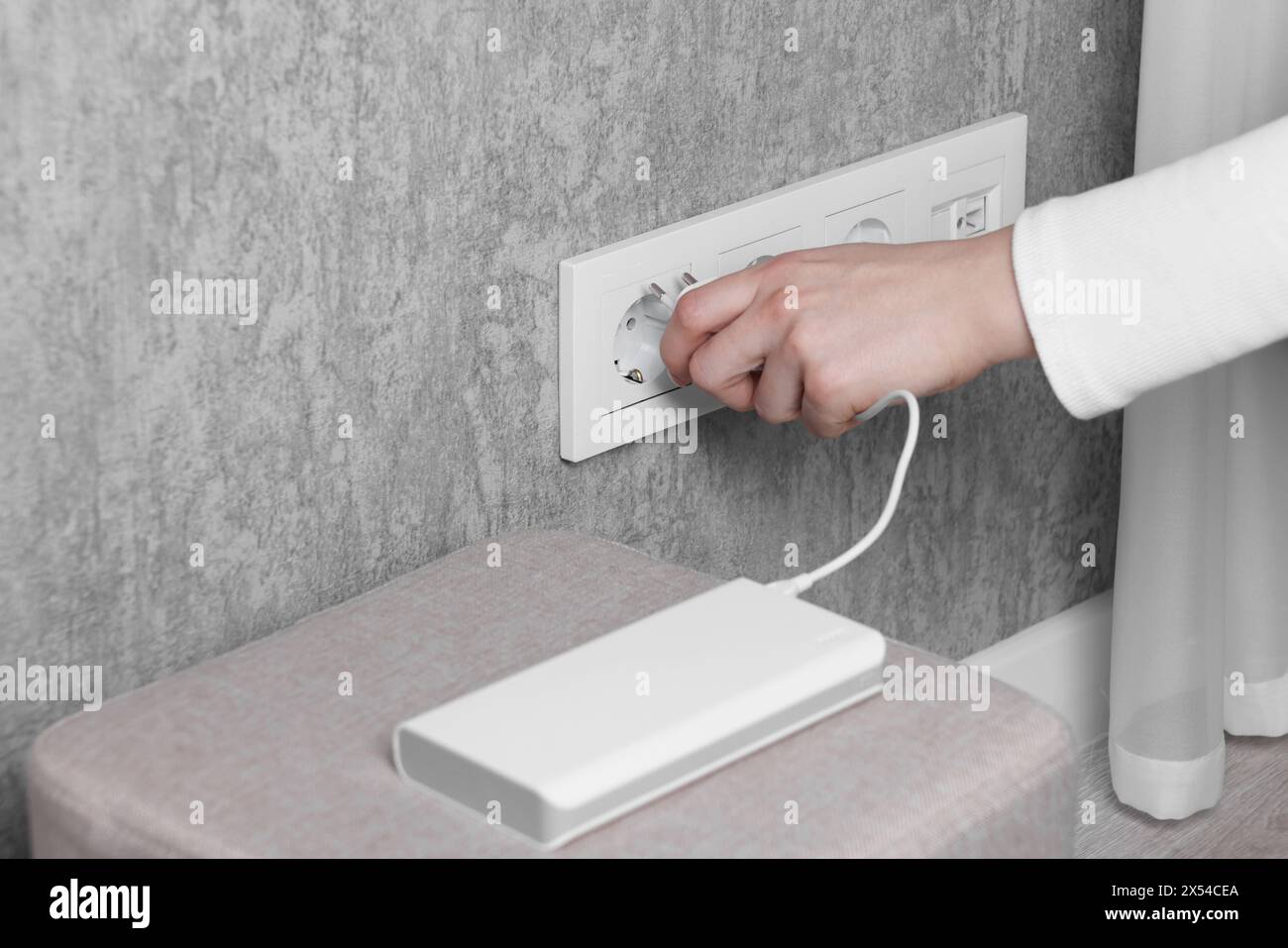 Woman plugging power bank into socket on grey wall indoors, closeup ...