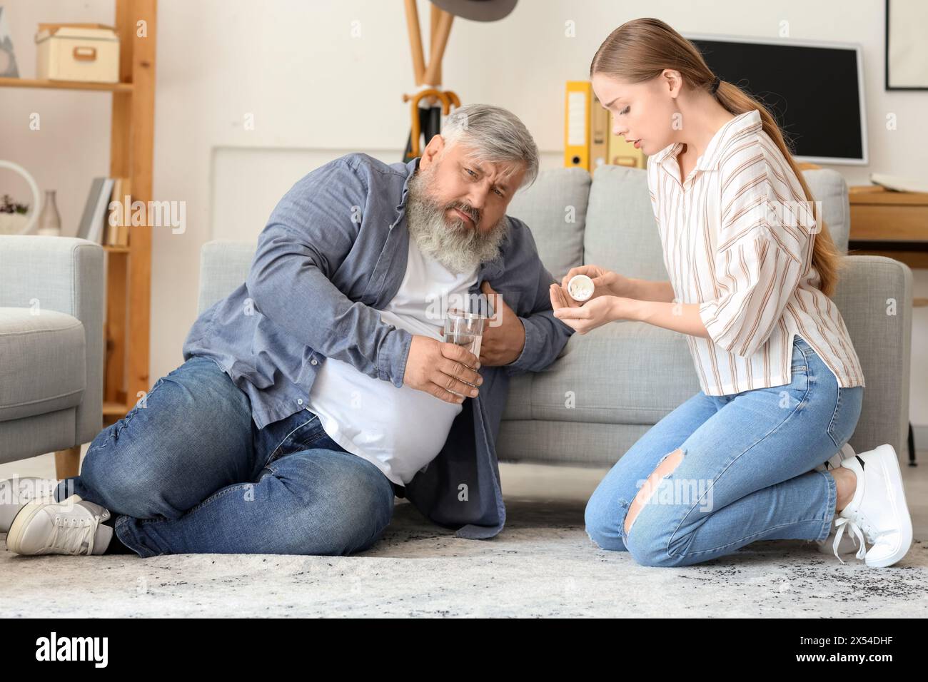Young woman giving medicine to her father who is having heart attack at ...