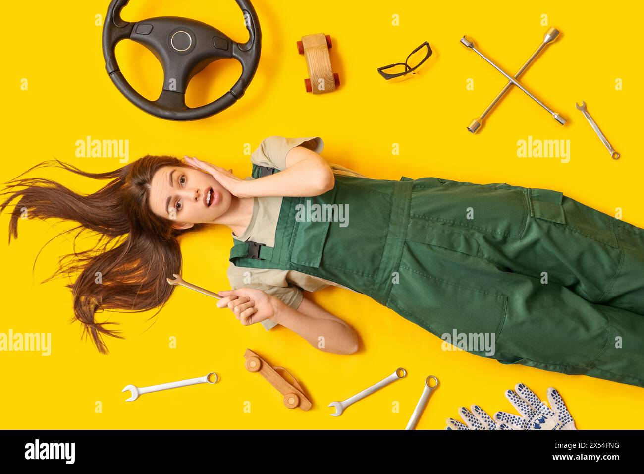 Surprised young female auto mechanic with different tools and steering ...