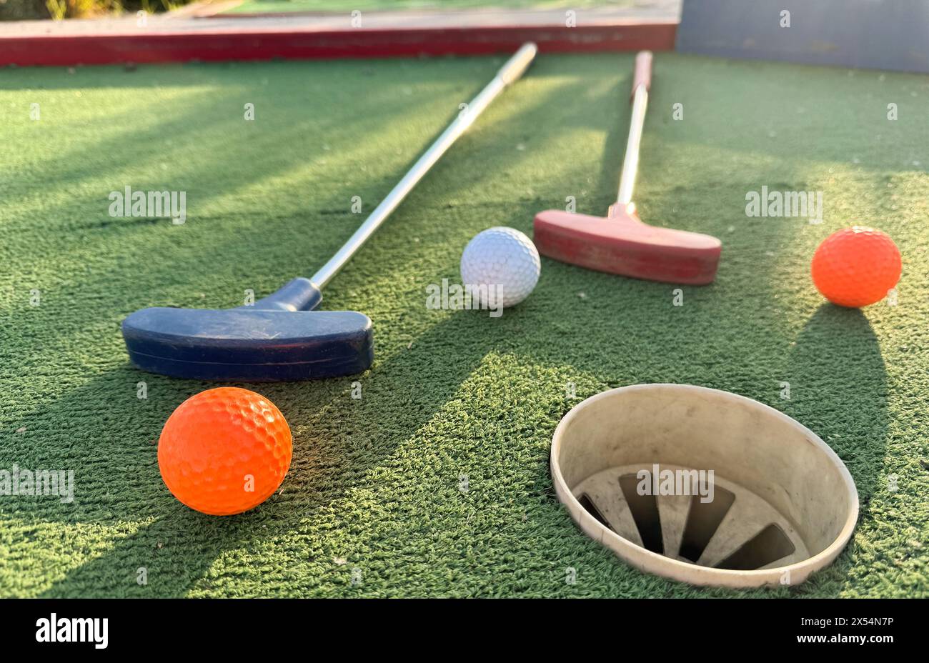 Mini-golf clubs and balls of different colors laid on artificial grass ...