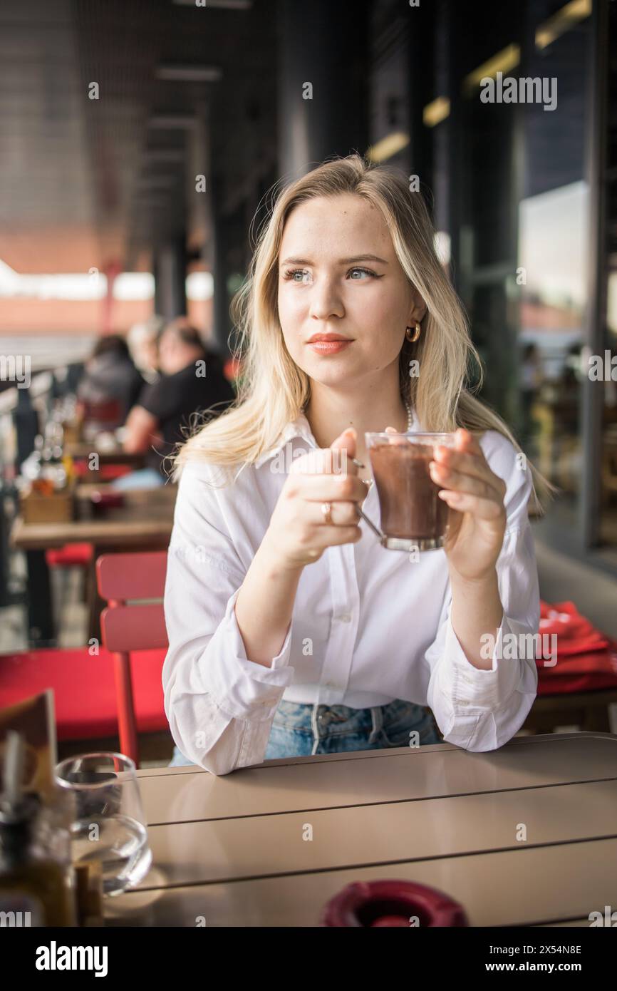 Gen z blonde woman drinks hot chocolate in summer cafe. Tasty beverage ...