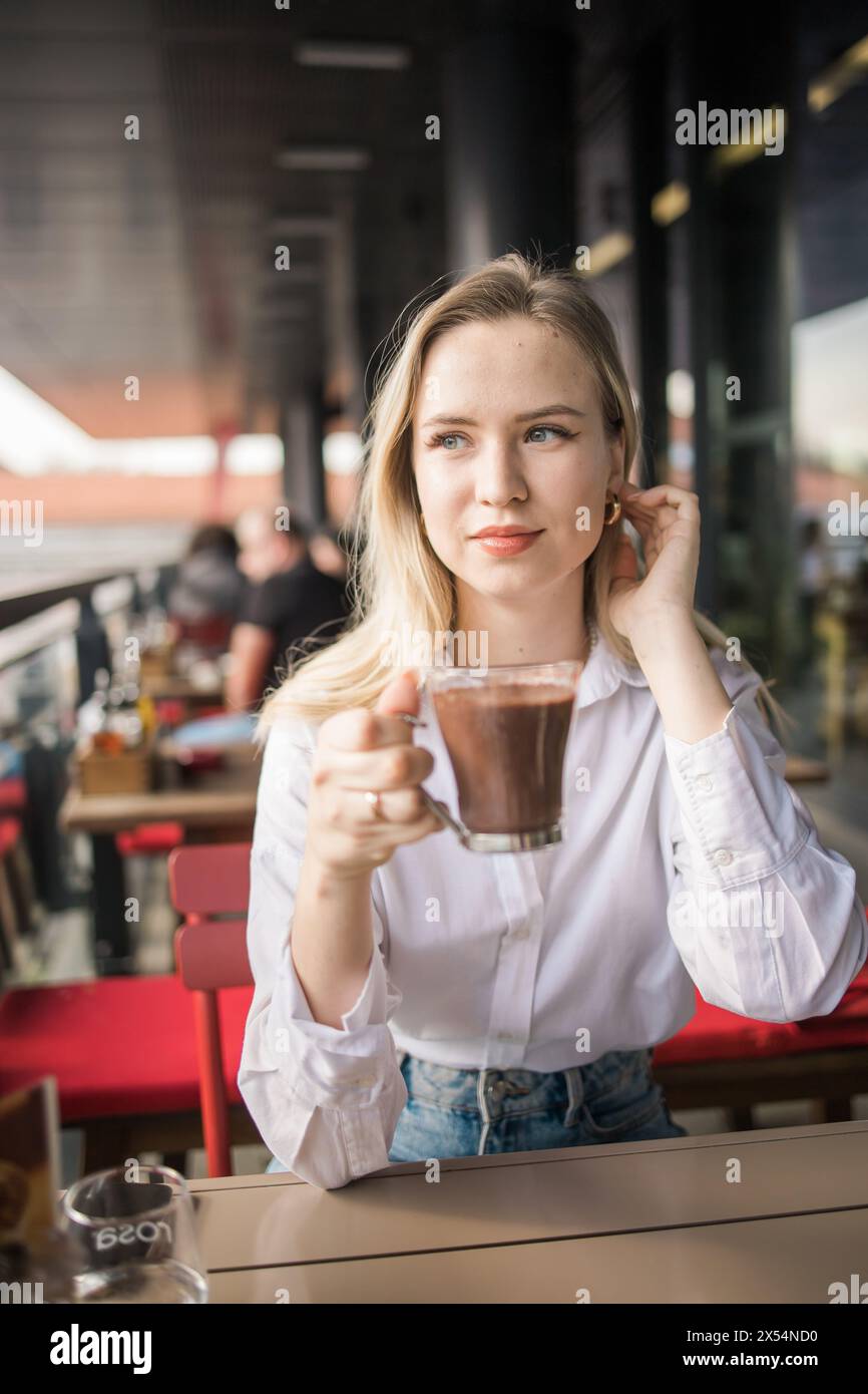 Gen z blonde woman drinks hot chocolate in summer cafe. Tasty beverage ...