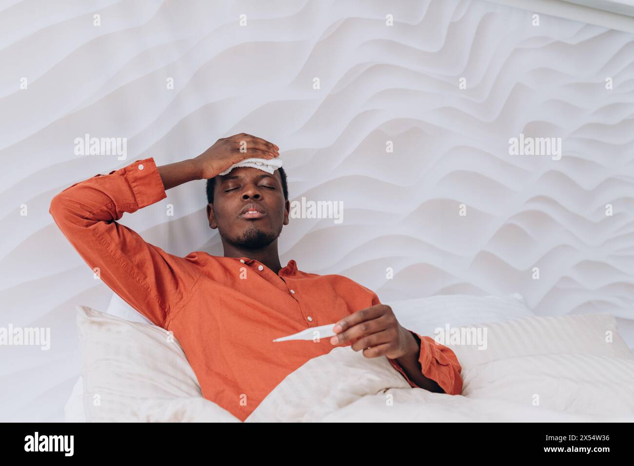 African American man lies in bed appearing unwell, holding a ...