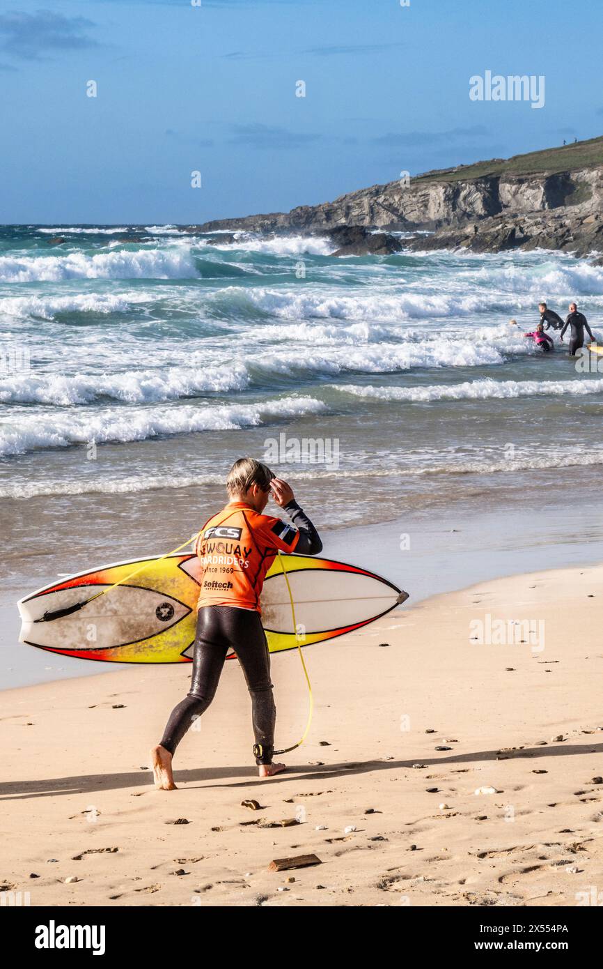 A young Grom surfer carrying his surfboard walking along the shoreline ...