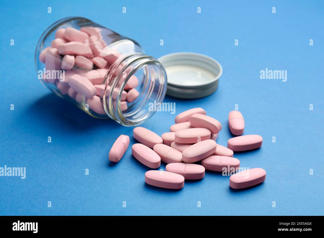 Bottle of pink vitamin capsules on blue background Stock Photo - Alamy