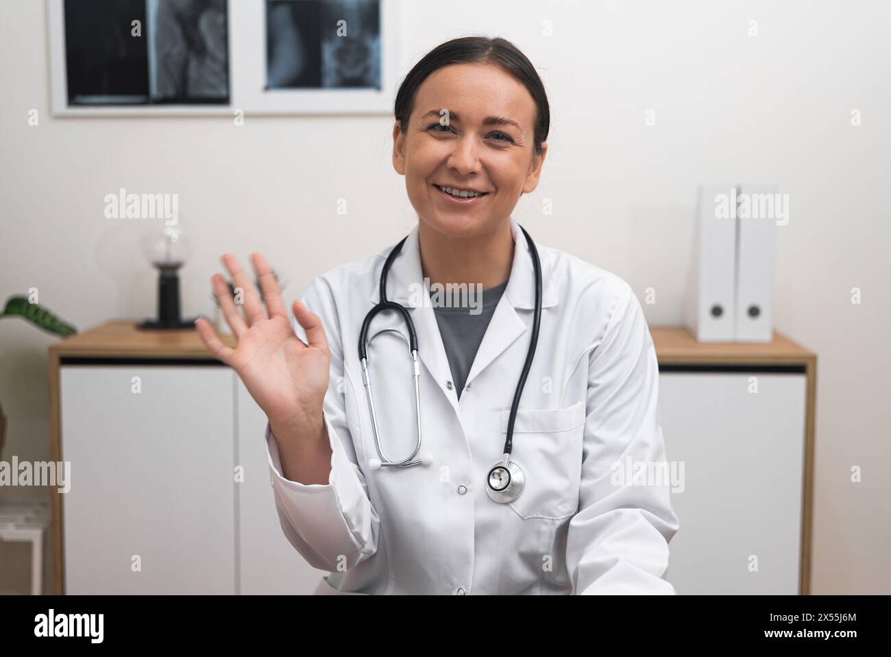 With smile, female doctor waving hand to camera, during online ...