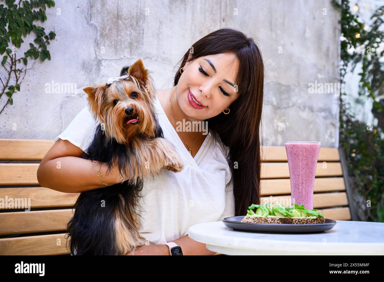 Cheerful lady with a dog sitting in an outdoor cafe, having a healthy ...