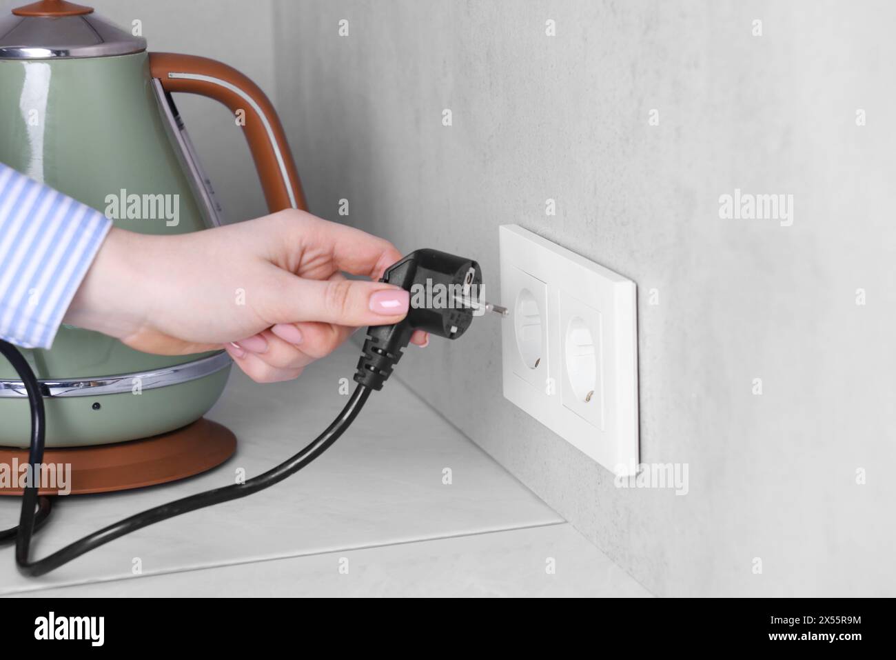 Woman plugging electric kettle into power socket at white table indoors ...