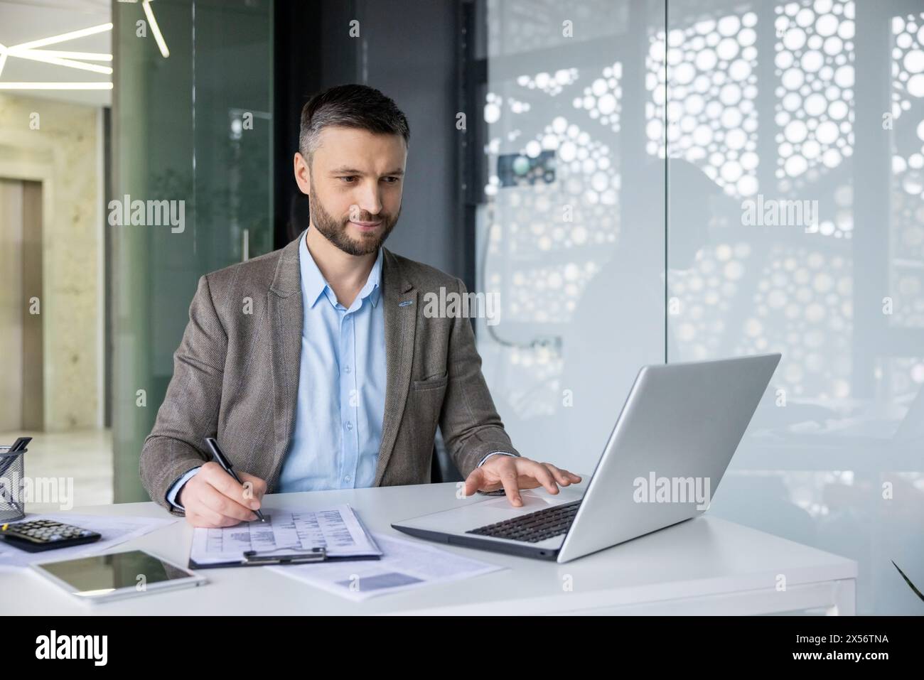 A focused business man reviewing documents while working on his laptop ...