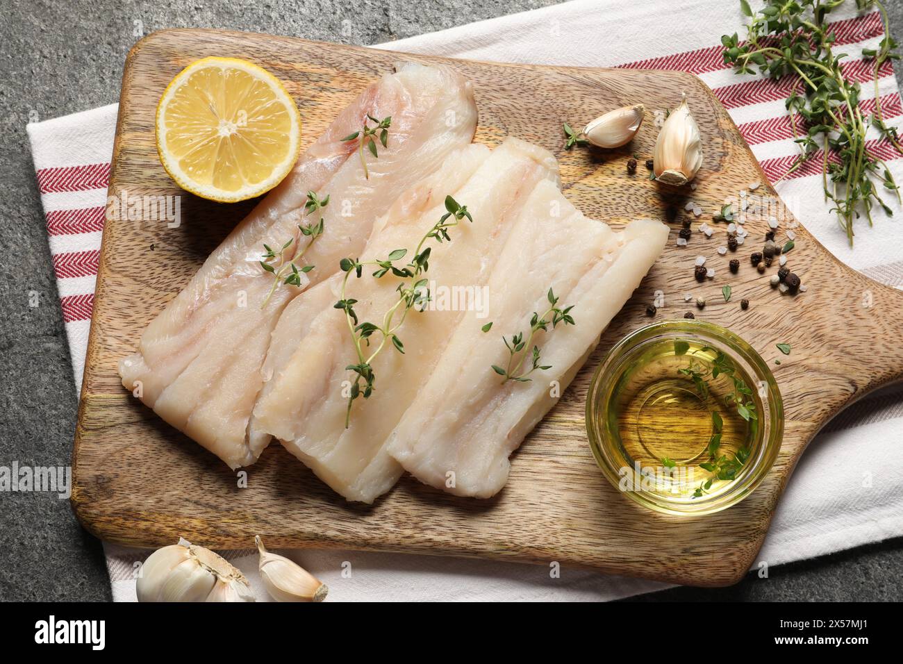 Raw cod fish, microgreens, lemon, spices and oil on grey textured table ...
