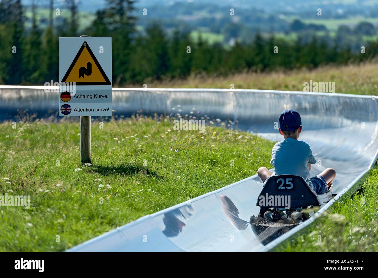 Boy with toboggan on the summer toboggan run, warning sign Attention ...