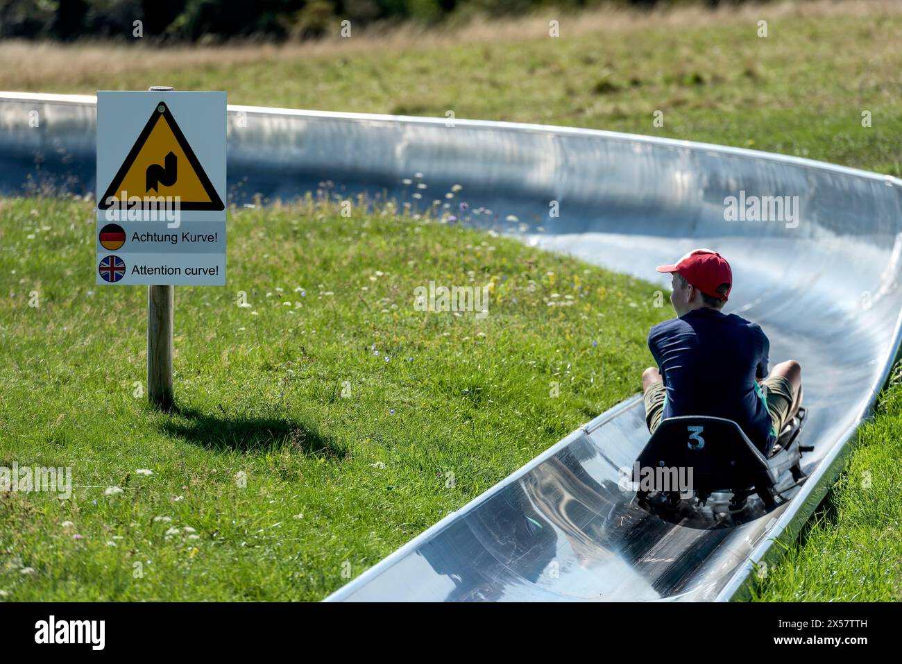 Boy with toboggan on the summer toboggan run, warning sign Attention ...