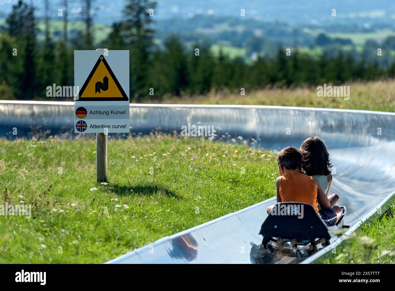 Boy and girl with sledges on the summer toboggan run, warning sign ...