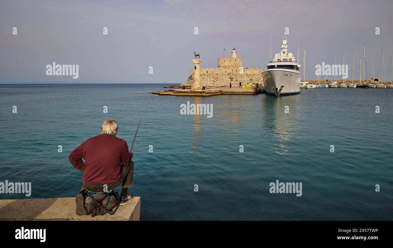 A man fishing on a shore with a view of an old fortress and a luxury ...