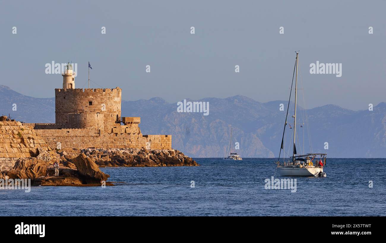 Sailing boat passes old fortress with lighthouse in soft morning light ...