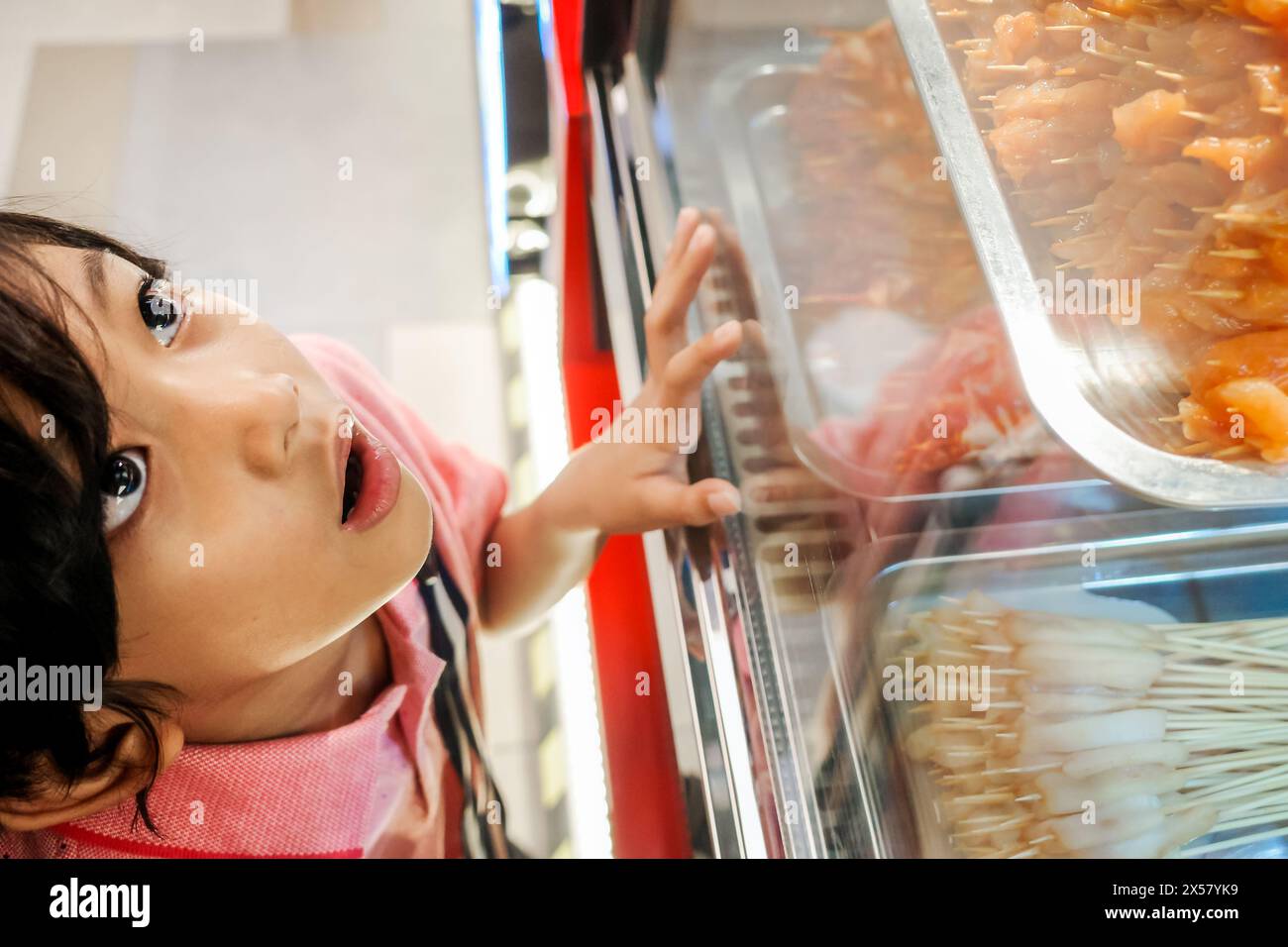 Southeast Asian little boy looking up on meals menu displayed at a ...