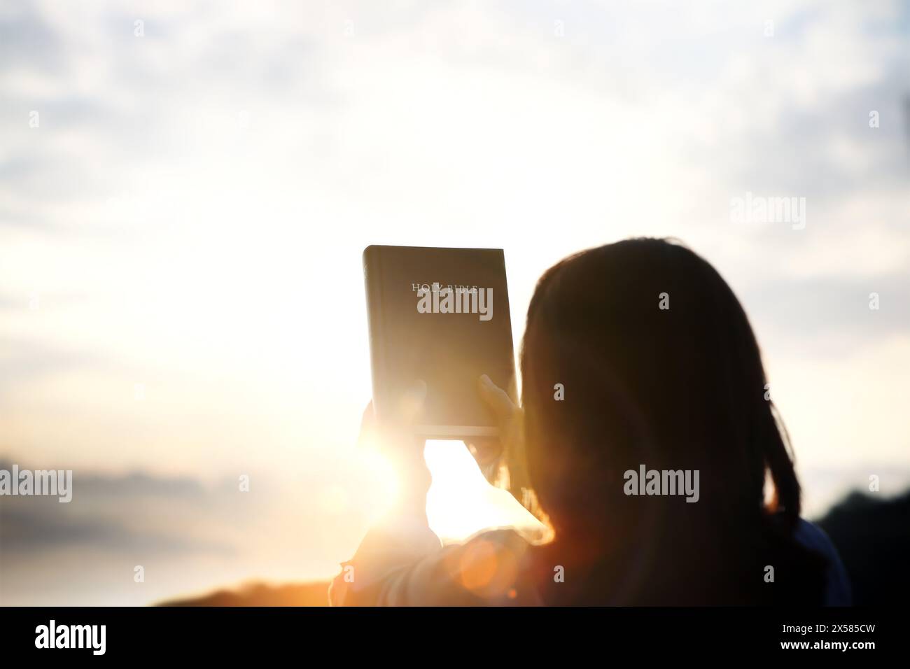 Christian woman holding high holy bible with sunset sky and bright ...