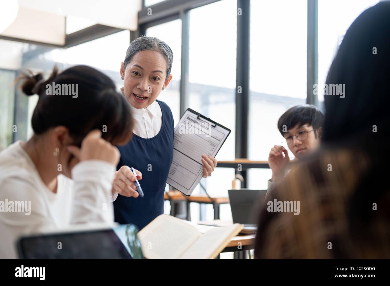 A mature Asian female teacher teaching students in the classroom ...