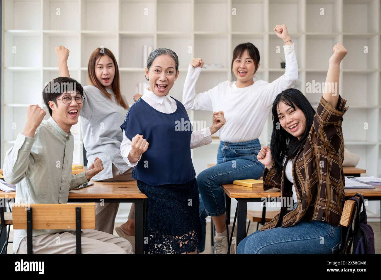 A cheerful mature Asian female teacher and students are showing fists ...