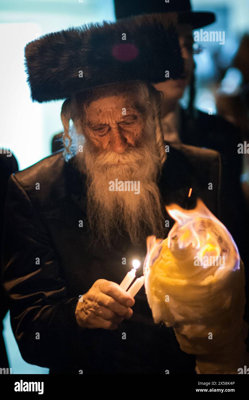 A bearded, elderly Jewish man wearing a streimel fur hat lights a ...