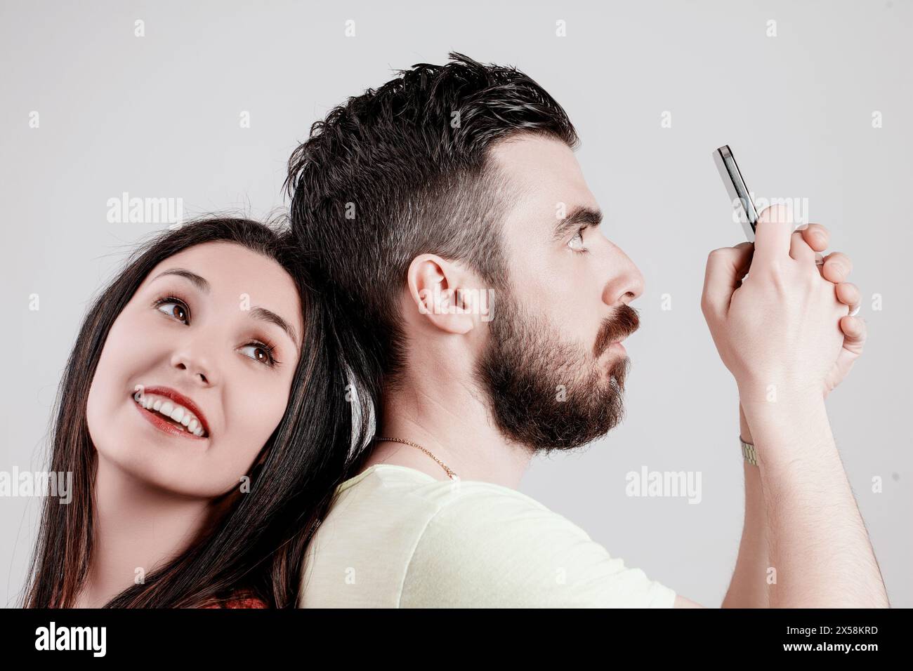 Young woman looks longingly at a man who is focused on his smartphone ...