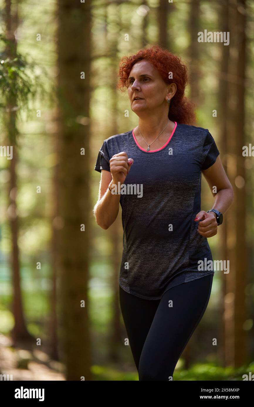 Redhead woman trail runner training in the forest running uphill Stock ...