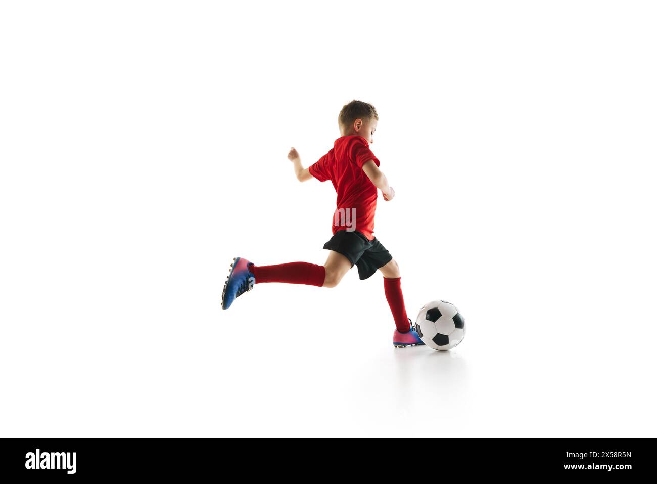 Sporty little boy, kicks ball to make perfect pass in motion against ...