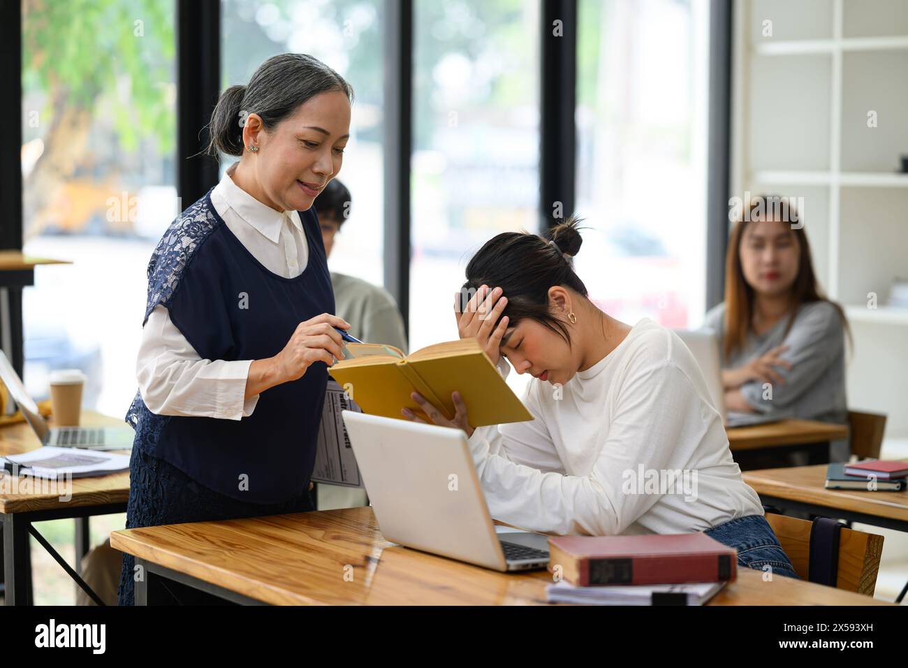 Middle age teacher assisting a struggling student with assignment in a ...