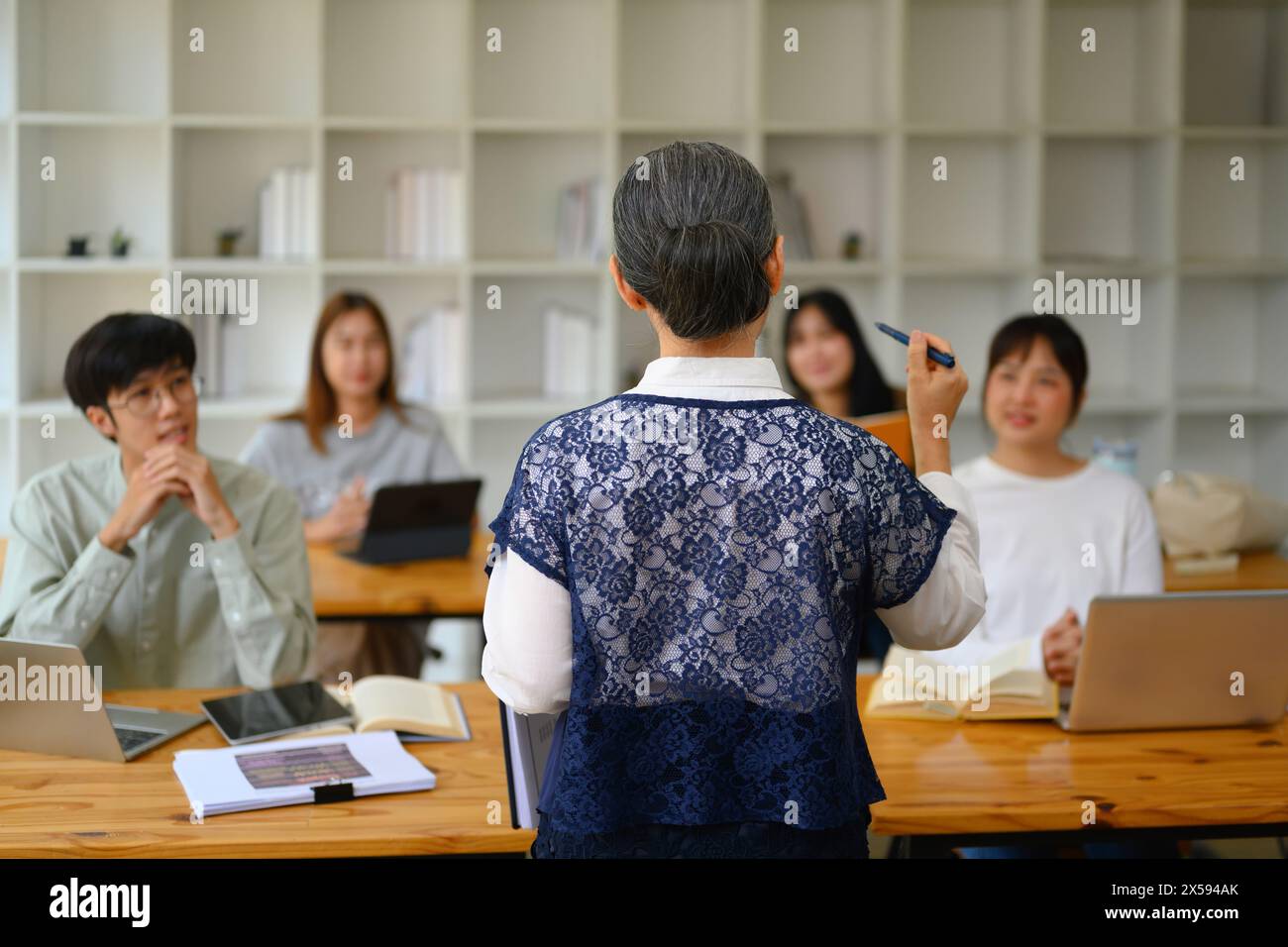 Rear view of senior professor talking to students during lecture in the ...