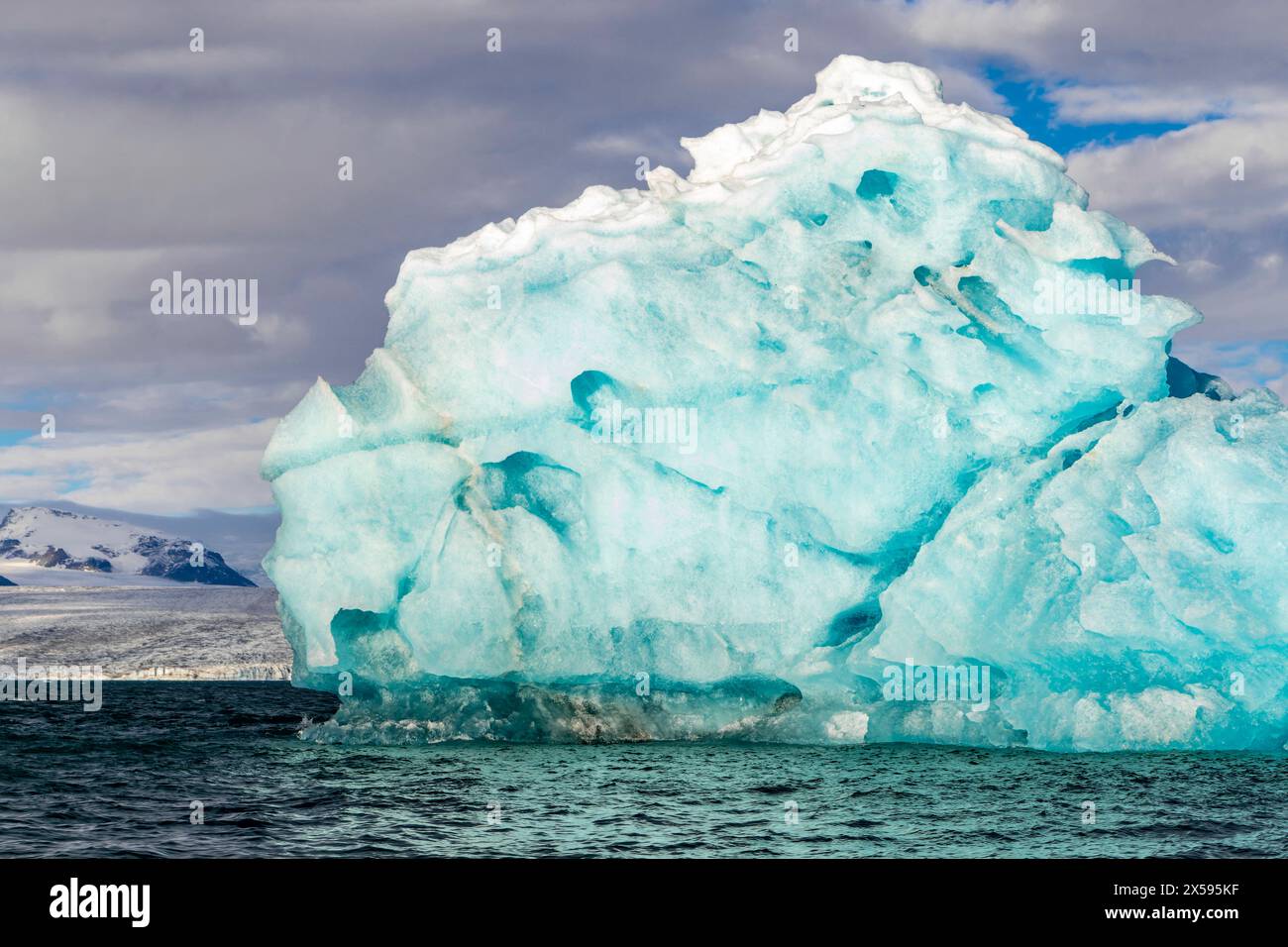 A large blue ice block floating in the ocean. The ice is surrounded by ...